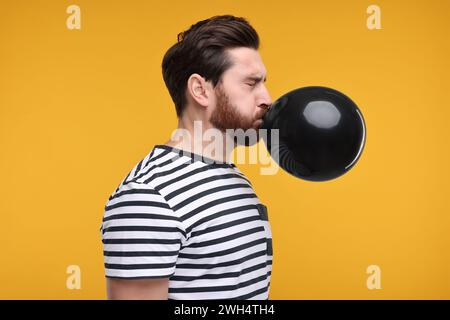 Man inflating black balloon on yellow background Stock Photo - Alamy