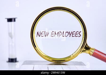 NEW EMPLOYEES Text written through a magnifying glass on a calculator ...