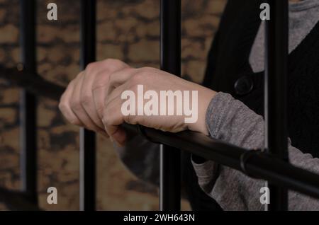The woman's hands rest on the iron bars of the prison cell, restricting ...