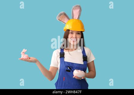 Female Asian worker in bunny ears with Easter eggs on blue background ...