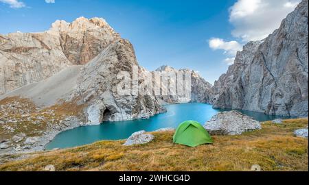 Green tent at the turquoise mountain lake Kol Suu with rocky steep ...