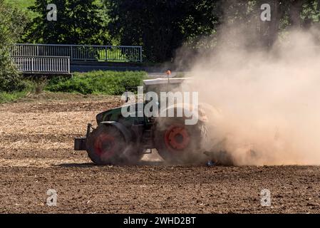 Tractor with plough digging up dried-out soil, large cloud of dust ...