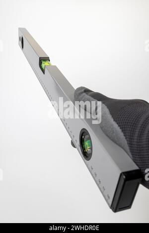 Man's hand holding a spirit level, gray, background white brick wall ...