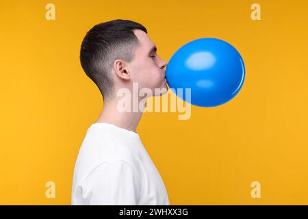 Young man inflating light blue balloon on yellow background Stock Photo ...