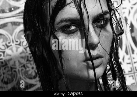 Sad and wet woman with smudged makeup on her face under the shower ...