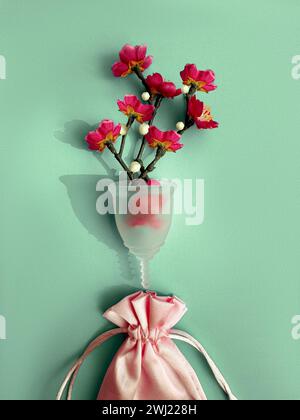 Menstrual cup with red flowers and pink silk bag, flat lay on purple ...