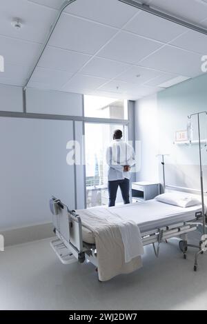 Thoughtful african american male doctor looking through window in ...
