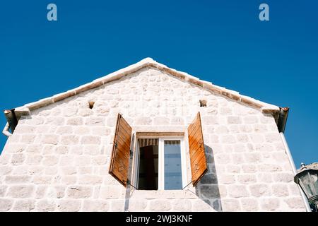 Open wide wooden shutters of the attic window of an ancient stone house ...