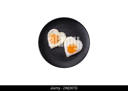 Two heart-shaped fried eggs on a black ceramic plate on a dark concrete ...
