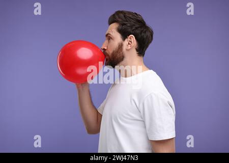 Man inflating red balloon on purple background Stock Photo - Alamy