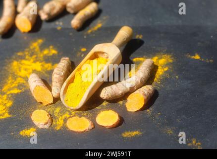 Turmeric powder (Kurkuma) in a wooden spoon and roots on a dark table ...