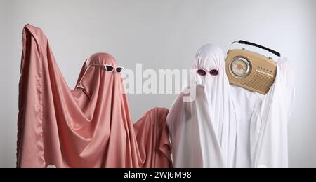 Glamorous ghosts. Women in color sheets with sunglasses on light grey ...