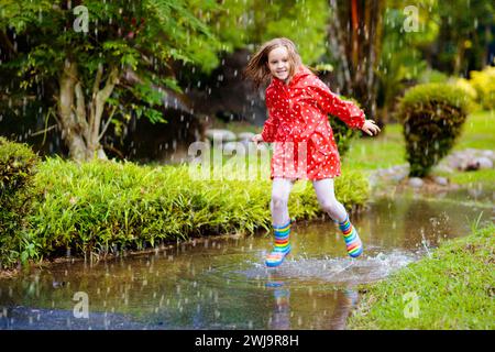 Child playing in puddle. Kids play and jump outdoor by autumn rain ...