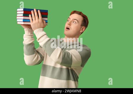 Emotional man holding stack of books on green background Stock Photo ...