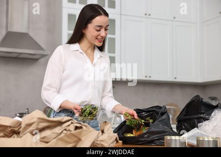 Garbage sorting. Woman putting food waste into plastic bag at table in ...