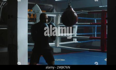Confident African American fighter hits punching bag while training in ...