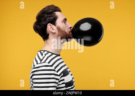 Man inflating black balloon on yellow background Stock Photo - Alamy