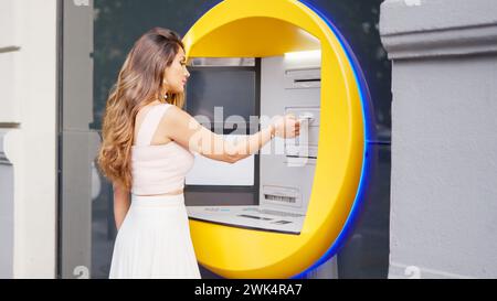 Young adult woman withdrawing money from an ATM cash machine outdoors ...
