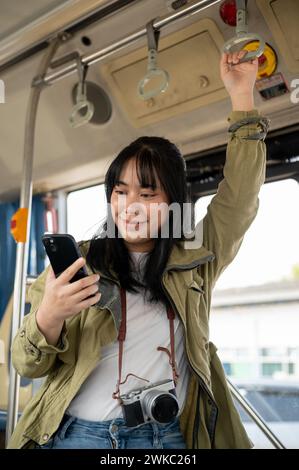 A positive Asian female solo traveler using her smartphone while ...