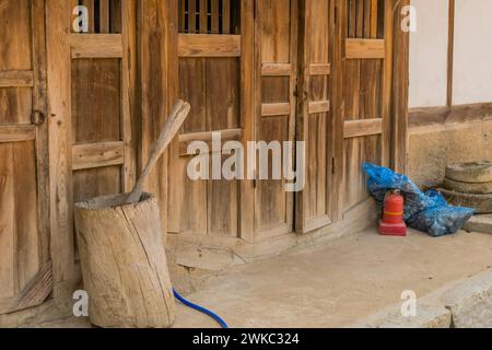 Wooden hand grain pulverizer in front of wooden building in public park ...