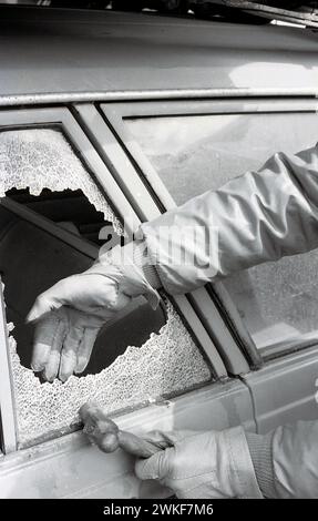 1970s, historical, a gloved hand car thief smashing a car window, a ...
