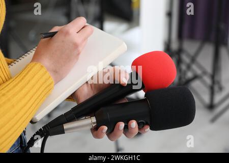 Professional journalist with microphones taking notes indoors, closeup ...