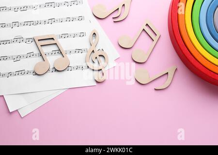 Baby songs. Music sheets, wooden notes and toy rainbow on pink ...