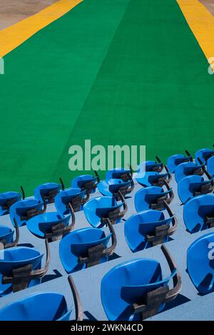 Empty blue folding spectator seats in front of synthetic green grass ...