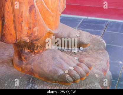 Coins laying on the feet of a wooden statue on top of plinth in South ...
