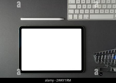 Tablet with blank screen, keyboard and supermarket cart on dark gray ...