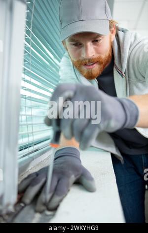 Handsome man using a screwdriver to install a window handle and looking ...