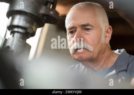 elderly worker watches processing of detail on milling machine Stock ...