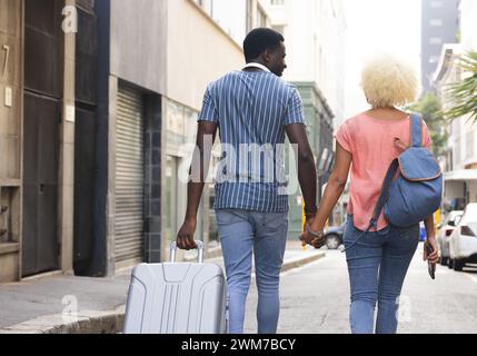 A young diverse biracial couple walks together outdoors, carrying ...