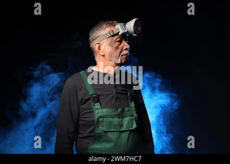 Mature miner man and blue smoke on black background Stock Photo - Alamy