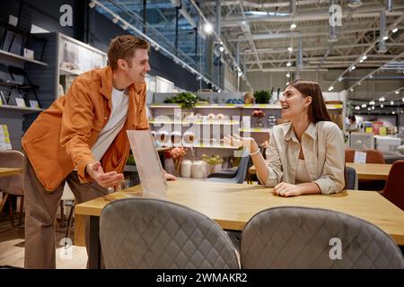 Positive loving couple testing new furniture for dining room at store ...