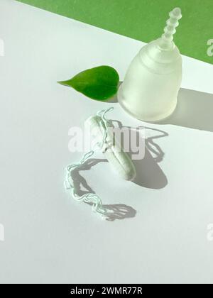 A reusable silicone menstrual cup and standard tampon on magenta paper ...