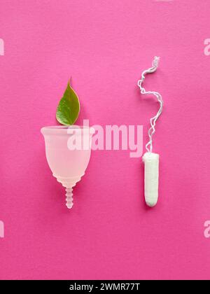 A reusable silicone menstrual cup and standard tampon on white and ...