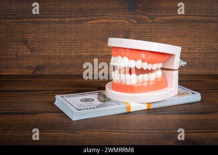 Banknotes in a pile, a model of teeth on top on wooden background ...