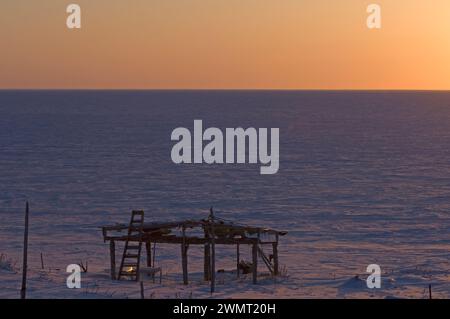 sunset over a wooden storage racks up off the ground for boat umiak ...