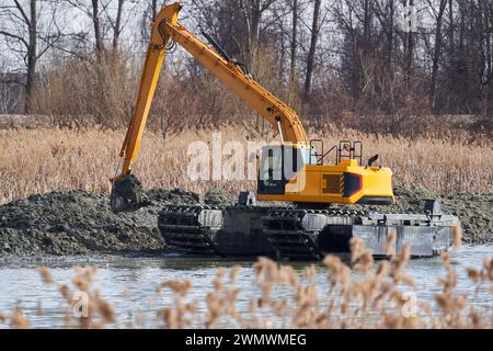 Earth digger, excavator, at the river's shore, working Stock Photo - Alamy