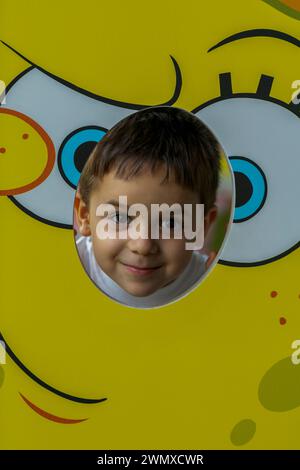 A young boy peers through a hole in the cheek of a Spongebob face ...