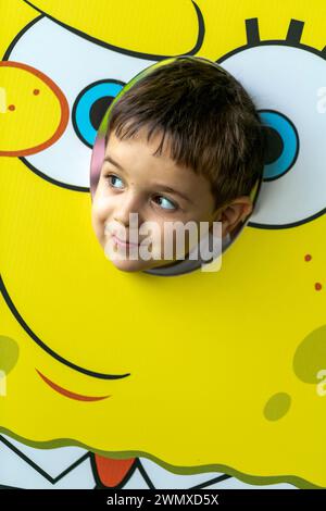 A young boy peers through a hole in the cheek of a Spongebob face ...