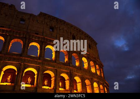 the wall of the colosseum with golden light at night in Rome, Italy ...