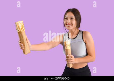 Sporty young Asian woman with doner kebab showing muscles on lilac ...