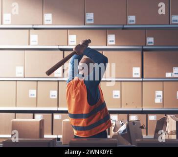 Angry rebellious worker smashing boxes with a bat on the conveyor belt ...