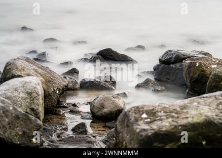 Cobblestones and rocks along the seacoast with smooth water through ...