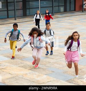 Happy tween schoolchildren with backpacks running to school outdoors ...