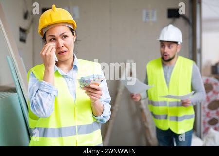 Crying construction workwoman standing at building site with banknotes ...