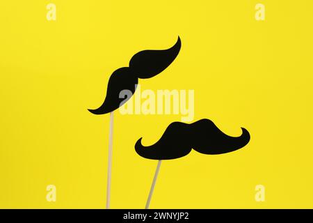 Fake paper mustaches with sticks on yellow background, flat lay. Space ...