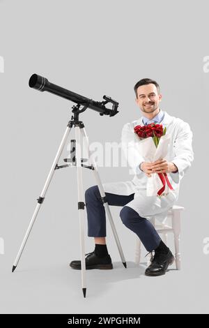 Happy male astronomer with bouquet of tulips and telescope on grey ...